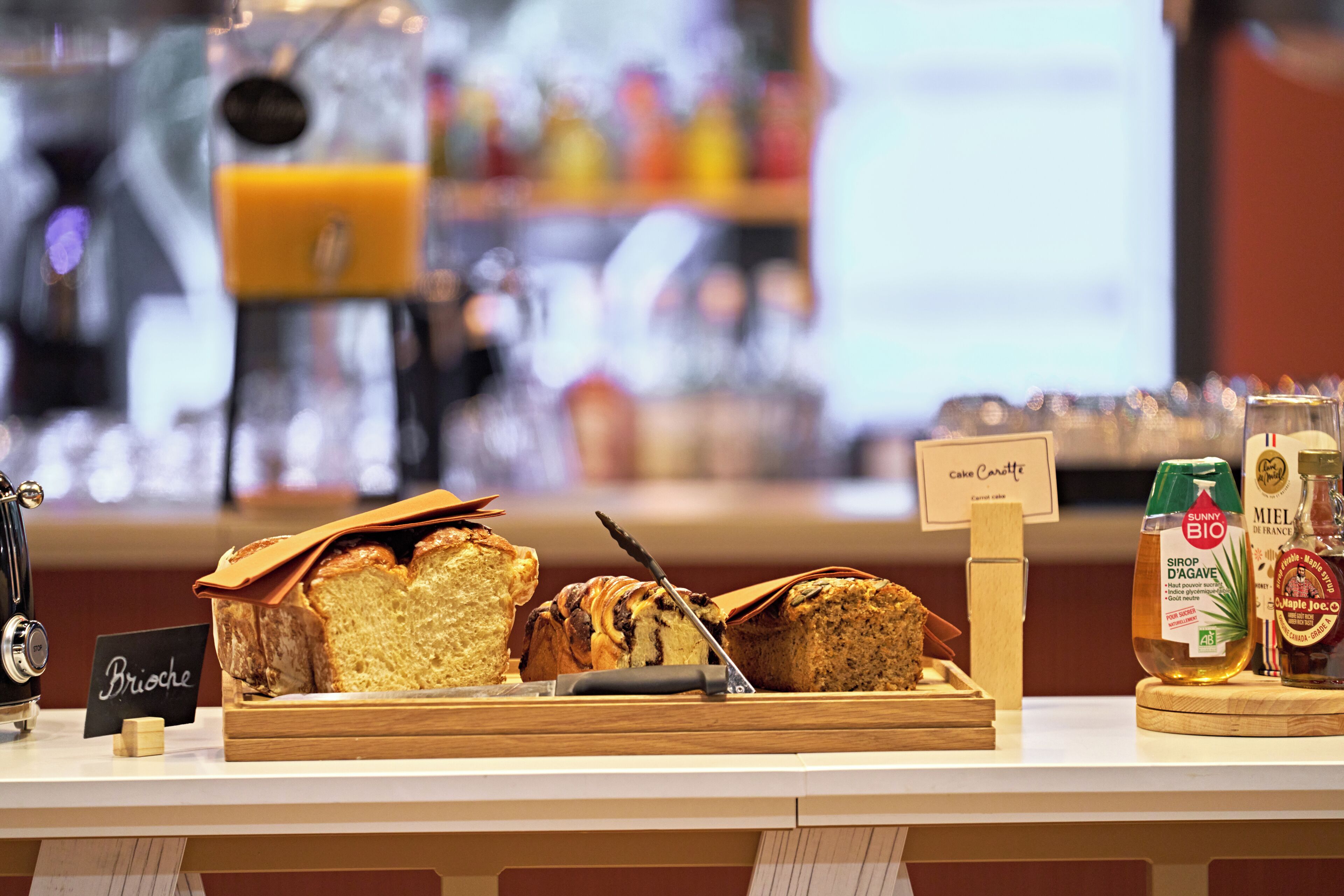 Um buffet de café da manhã com diversos pães e doces, uma máquina de café e seleção de bebidas.