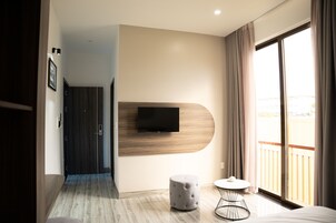 Quarto de hotel moderno com uma grande janela, televisão de tela plana na parede, um banquinho redondo e uma pequena mesa redonda.