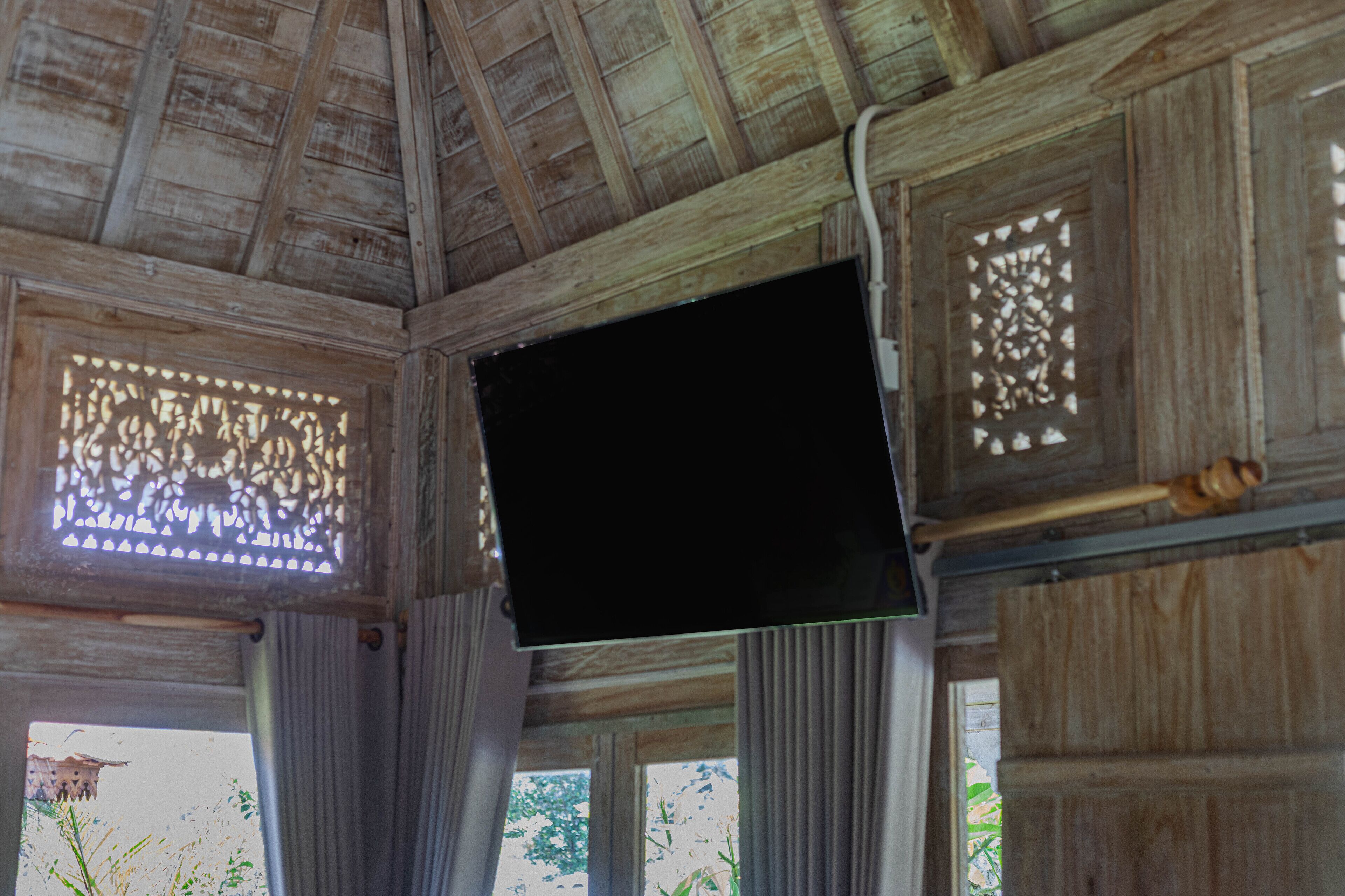 Quarto com teto de madeira, TV fixada na parede e janela com divisória decorativa.