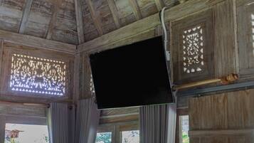 Quarto com teto de madeira, TV fixada na parede e janela com divisória decorativa.