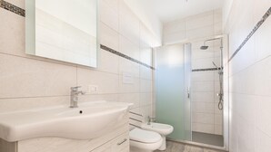 Uma casa de banho moderna com uma grande pia, duas sanitas e zona de duche com paredes de vidro.
