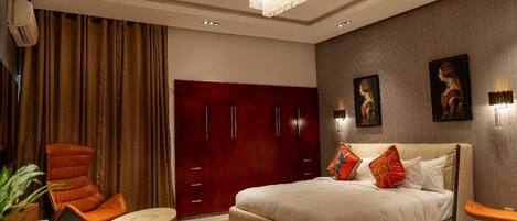 Quarto moderno com uma cama grande, um guarda-roupa de madeira, uma poltrona de couro e uma mesinha.