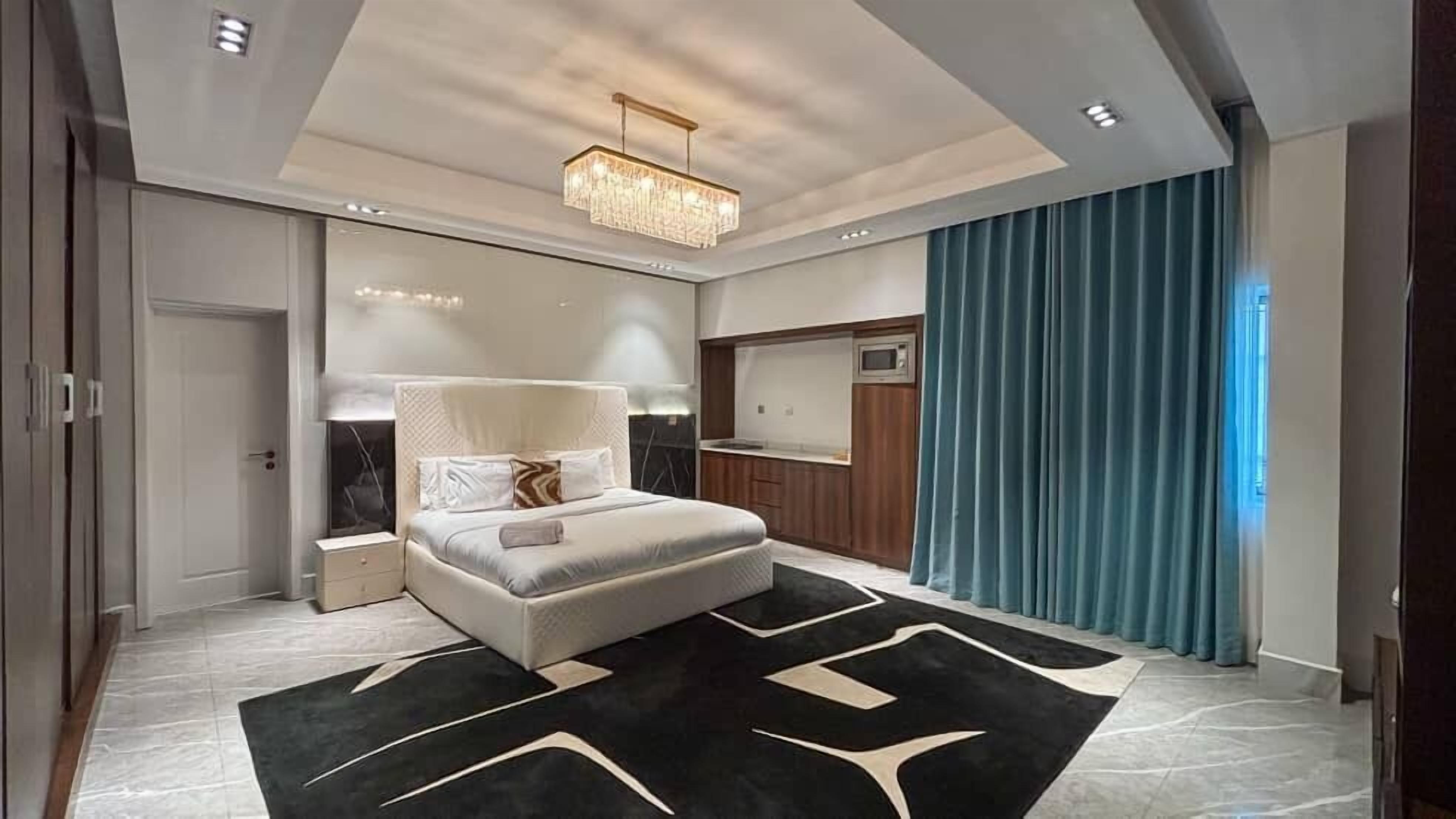 Quarto moderno com cama grande, escrivaninha embutida e janela ampla com cortinas.