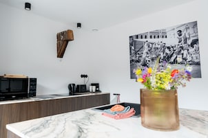 Uma cozinha moderna com bancada de mármore, micro-ondas, cafeteira e um vaso de flores.