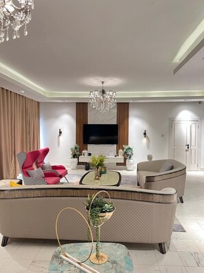 Uma sala de estar moderna com um sofá grande, duas poltronas, uma mesa de centro e uma televisão.
