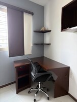 Escritório de canto com mesa, cadeira e estante.