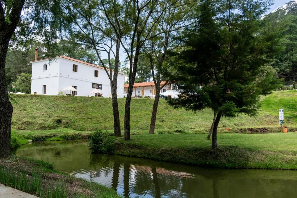 Um edifício branco com telhado vermelho, rodeado de árvores e um pequeno lago.