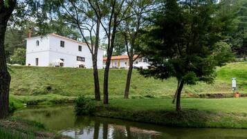 Um edifício branco com telhado vermelho, rodeado de árvores e um pequeno lago.