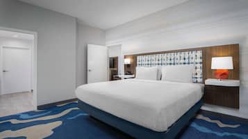 Quarto de hotel moderno, com uma cama grande, uma mesa de cabeceira e uma luminária, e um banheiro visível por uma porta aberta.