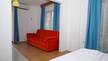 Um quarto com uma cama, um sofá vermelho e uma janela com cortinas azuis.