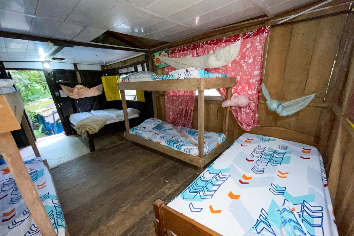 Quarto em dormitório com beliches, piso de madeira e janela com cortinas.