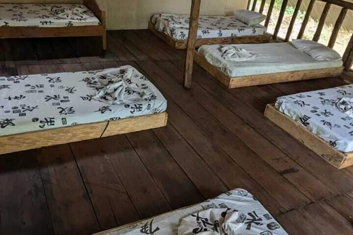 Um quarto em dormitório com piso de madeira e beliches, cada um com um colchão apresentando texto em preto.