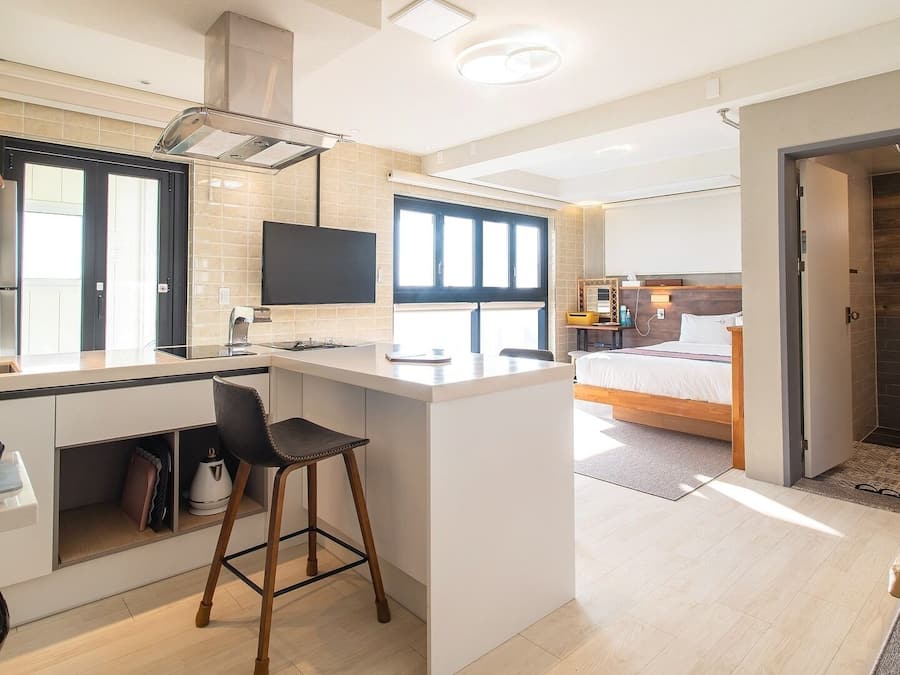 Cozinha compacta com ilha central, área de jantar e um quarto com janela grande.