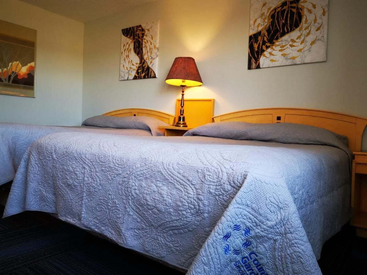 Quarto de hotel com duas camas, uma luminária e obras de arte nas paredes.