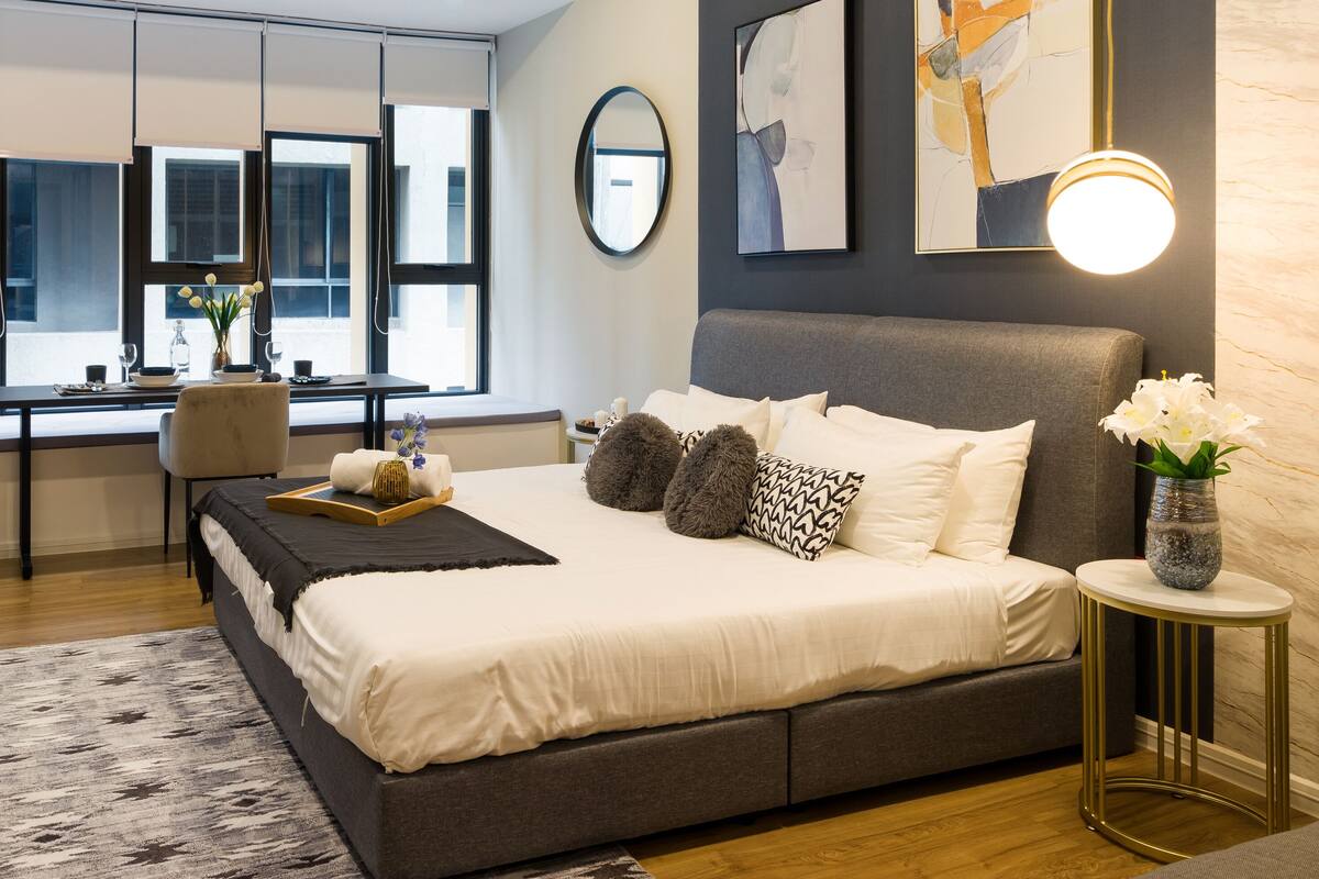 Um quarto moderno com uma cama grande, mesas de cabeceira, uma escrivaninha e uma janela com persianas.