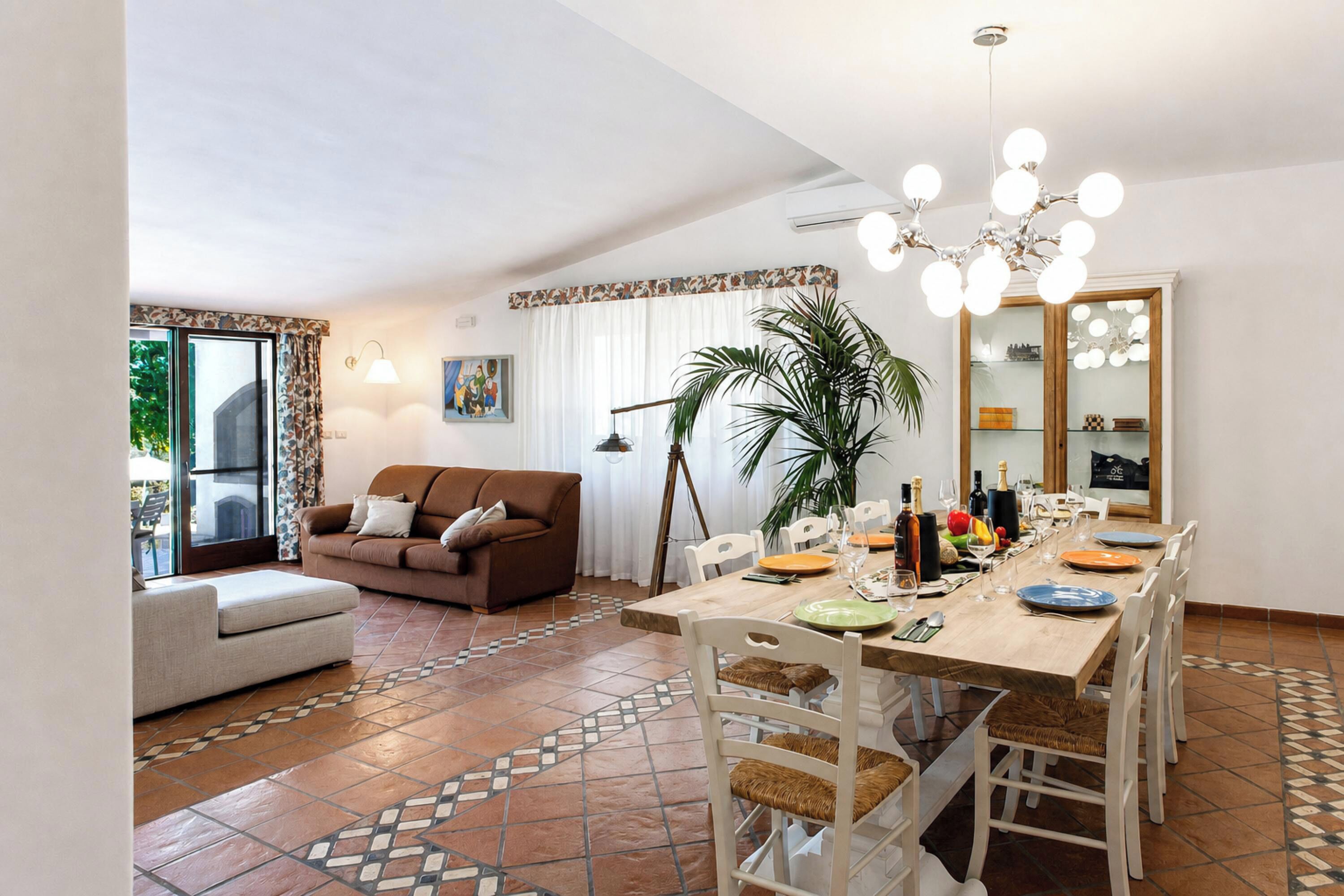 Uma sala de jantar com mesa de madeira, cadeiras brancas e um candelabro.