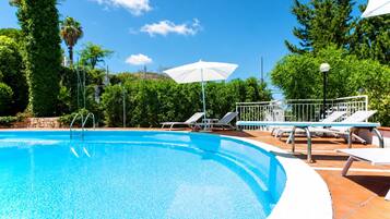 Piscina com espreguiçadeiras e guarda-sóis, rodeada por vegetação e céu claro.