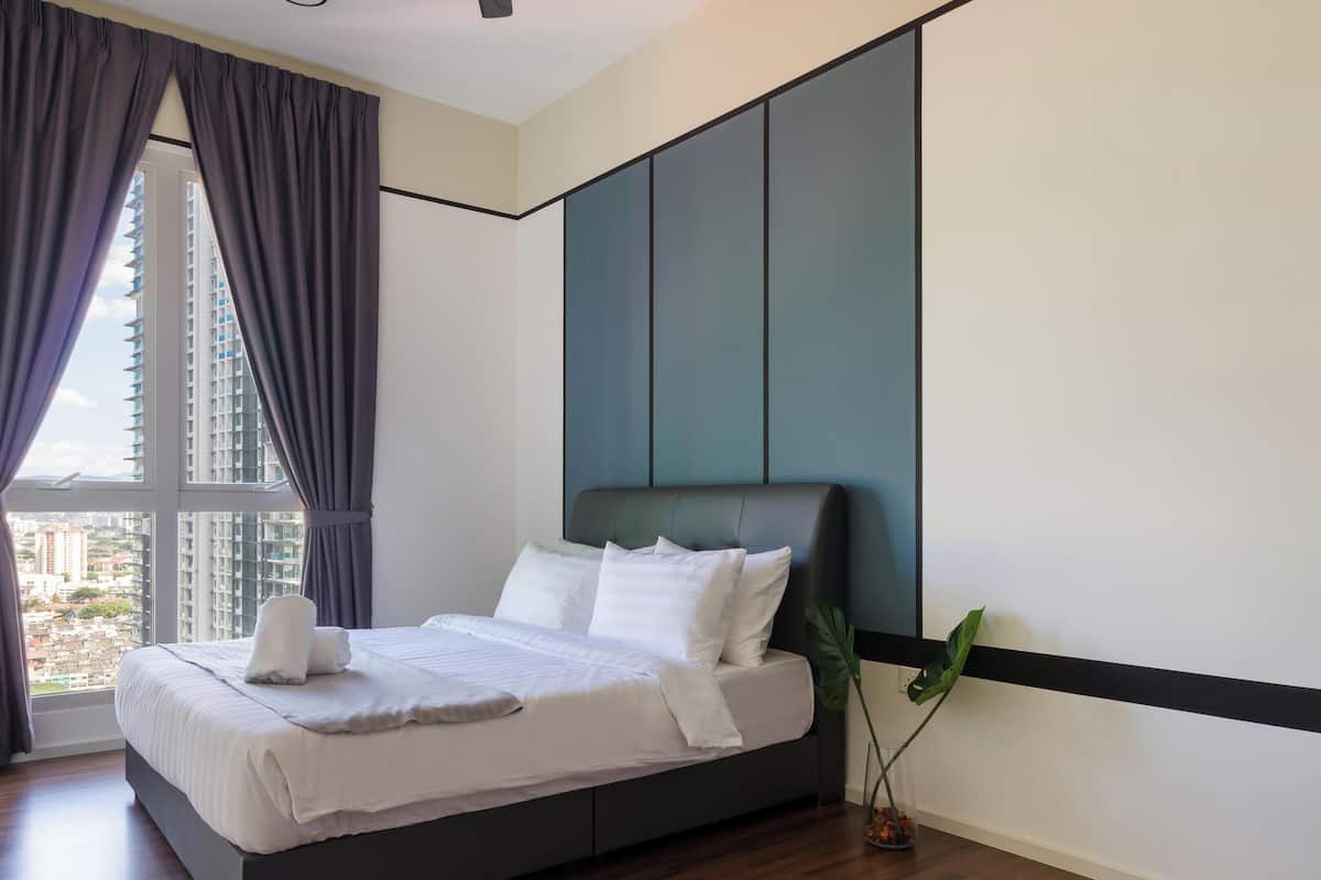 Quarto moderno com uma janela grande, cama com roupa de cama branca, cabeceira escura e um vaso com planta.