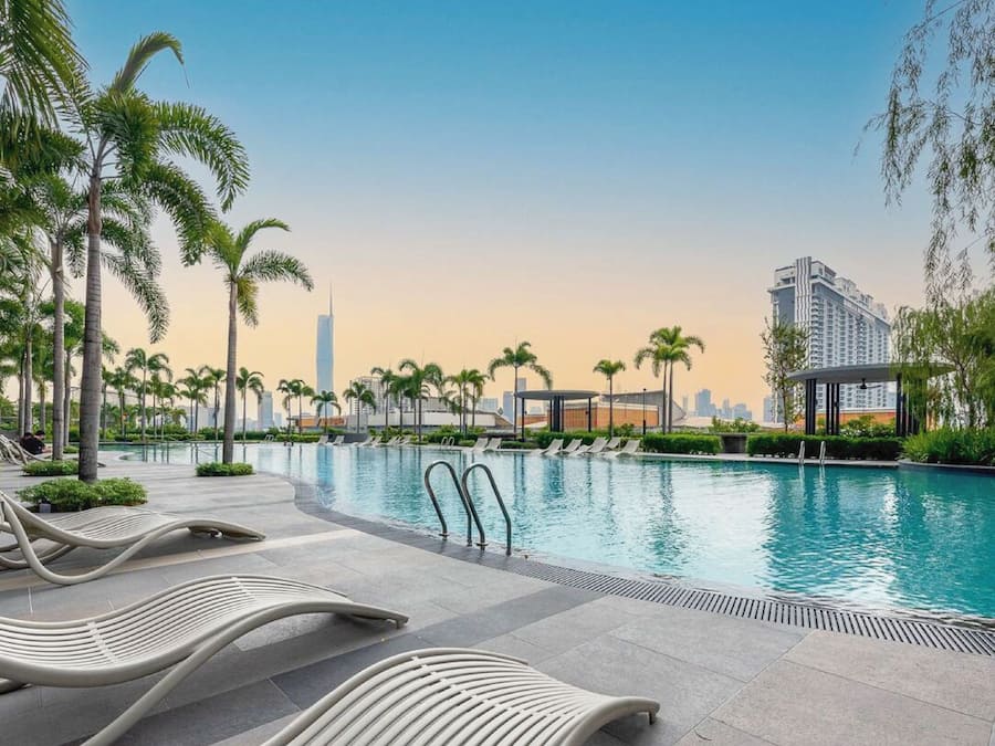 Uma área de piscina moderna com espreguiçadeiras, palmeiras e vista para o horizonte urbano.