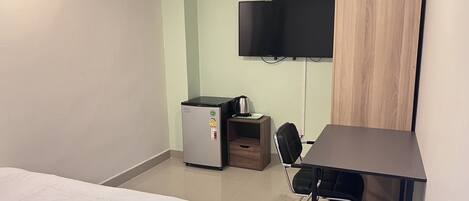Quarto de hotel com cama, escrivaninha, cadeira, televisão e frigorífico.