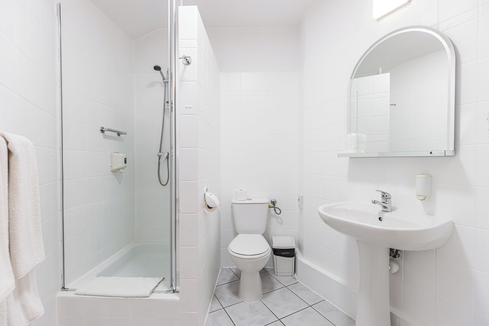 Casa de banho moderna com chuveiro envidraçado, sanita branca e lavatório com espelho.