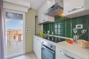 Cozinha moderna com porta de vidro deslizante, coifa de aço inoxidável e backsplash com azulejos verdes.