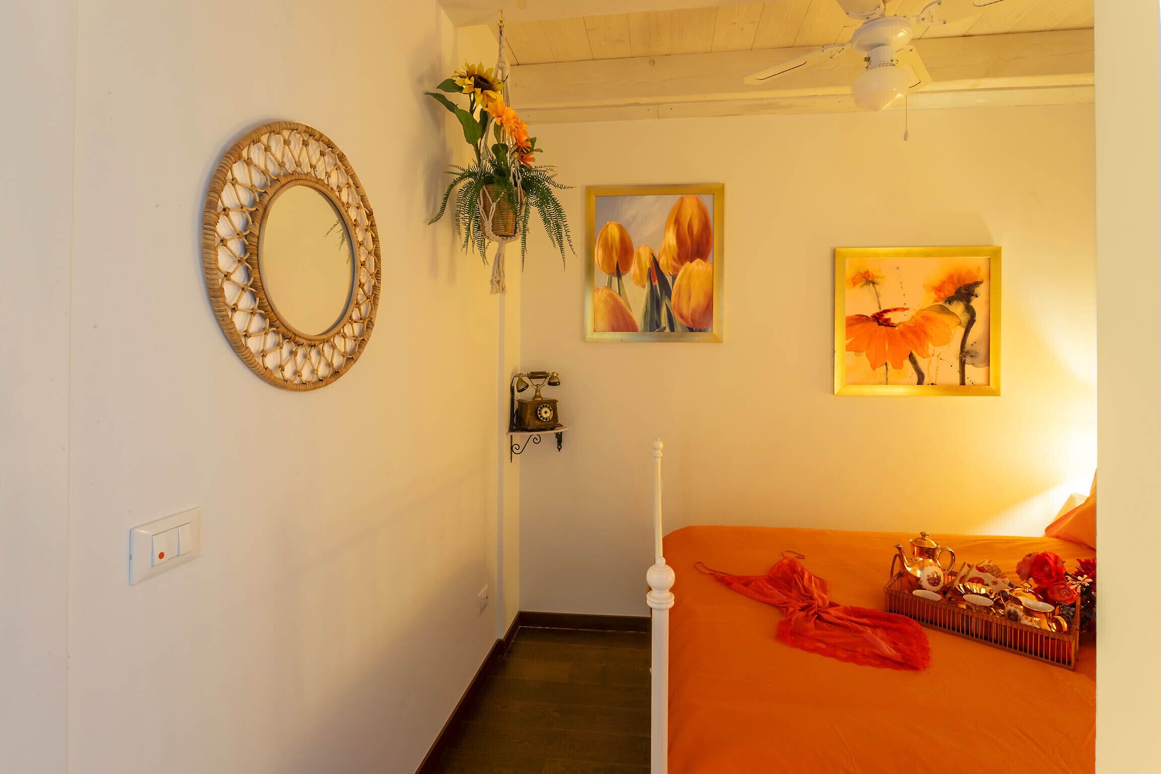 Quarto com cama, espelho fixado na parede e duas pinturas emolduradas.