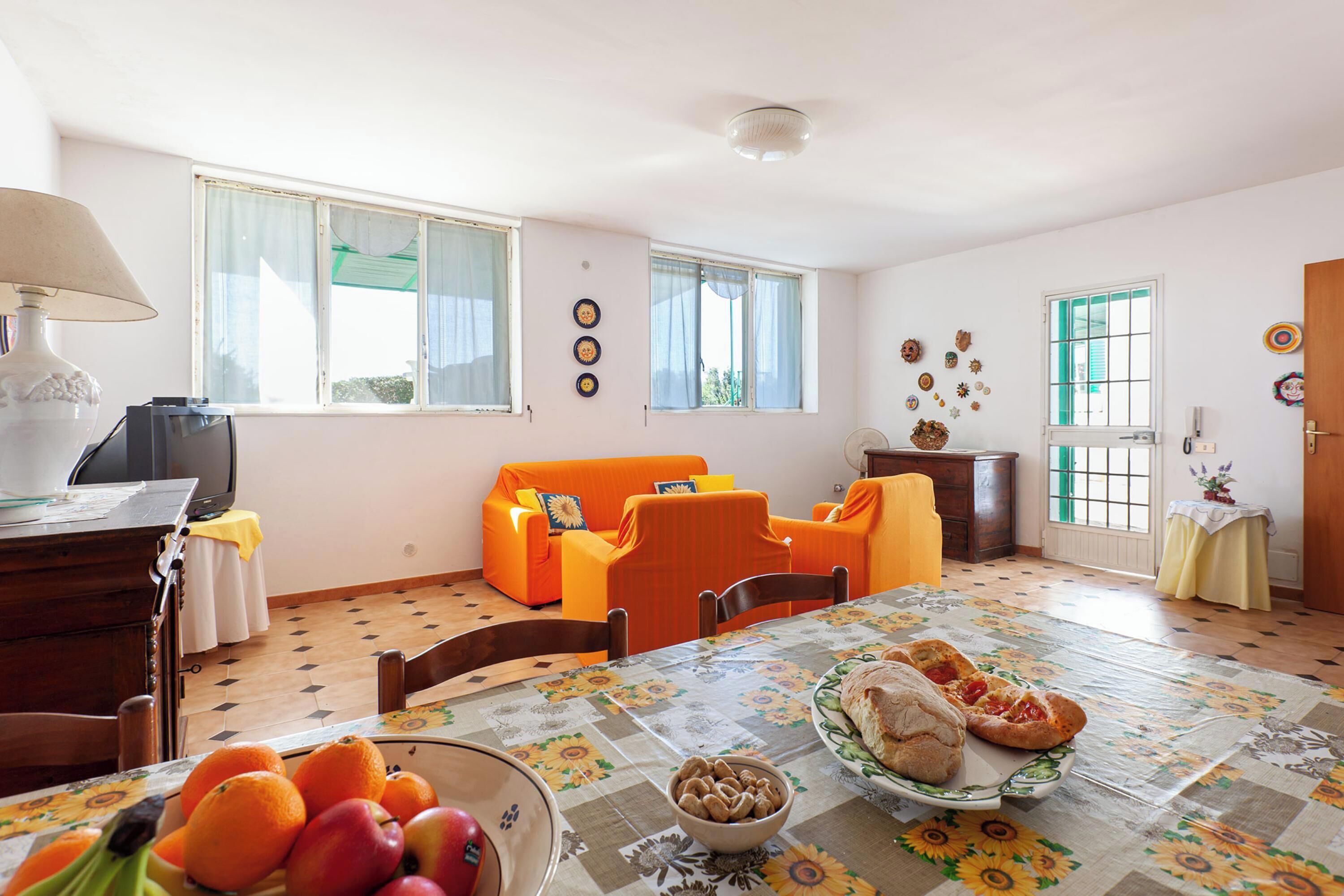 Uma área de refeições com uma mesa posta para dois, um sofá e uma televisão no canto.