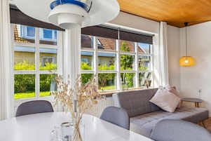 Uma sala de estar moderna com uma janela ampla, um sofá, uma mesa de jantar e uma luminária pendente.