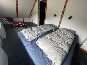 Quarto com duas camas, uma cadeira vermelha e teto de madeira.
