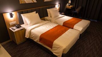 Quarto de hotel com duas camas, uma mesa de cabeceira com telefone, luminária e uma cadeira.