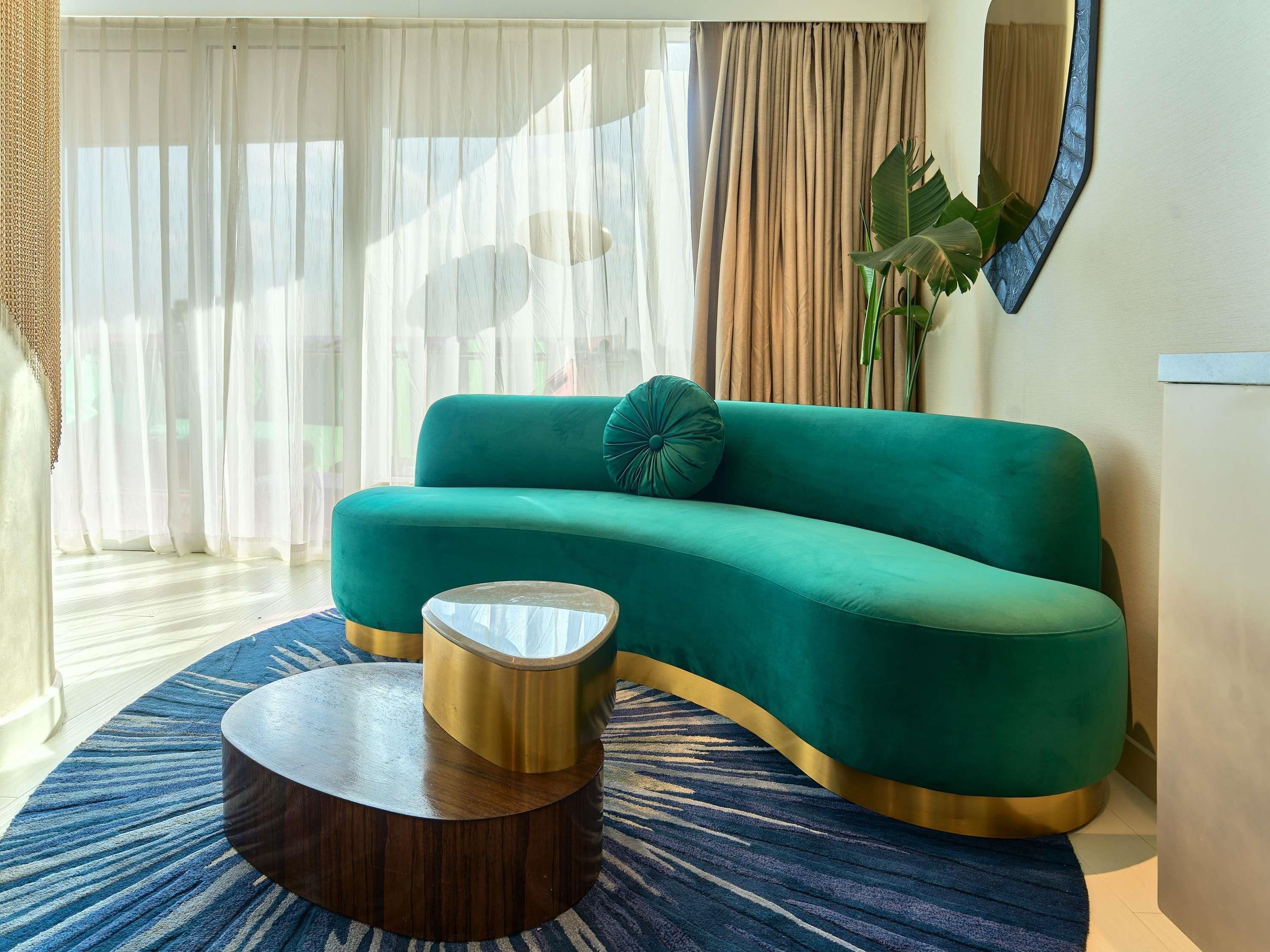Um quarto com um sofá verde curvo, uma mesa de centro de madeira redonda e um tapete azul estampado.