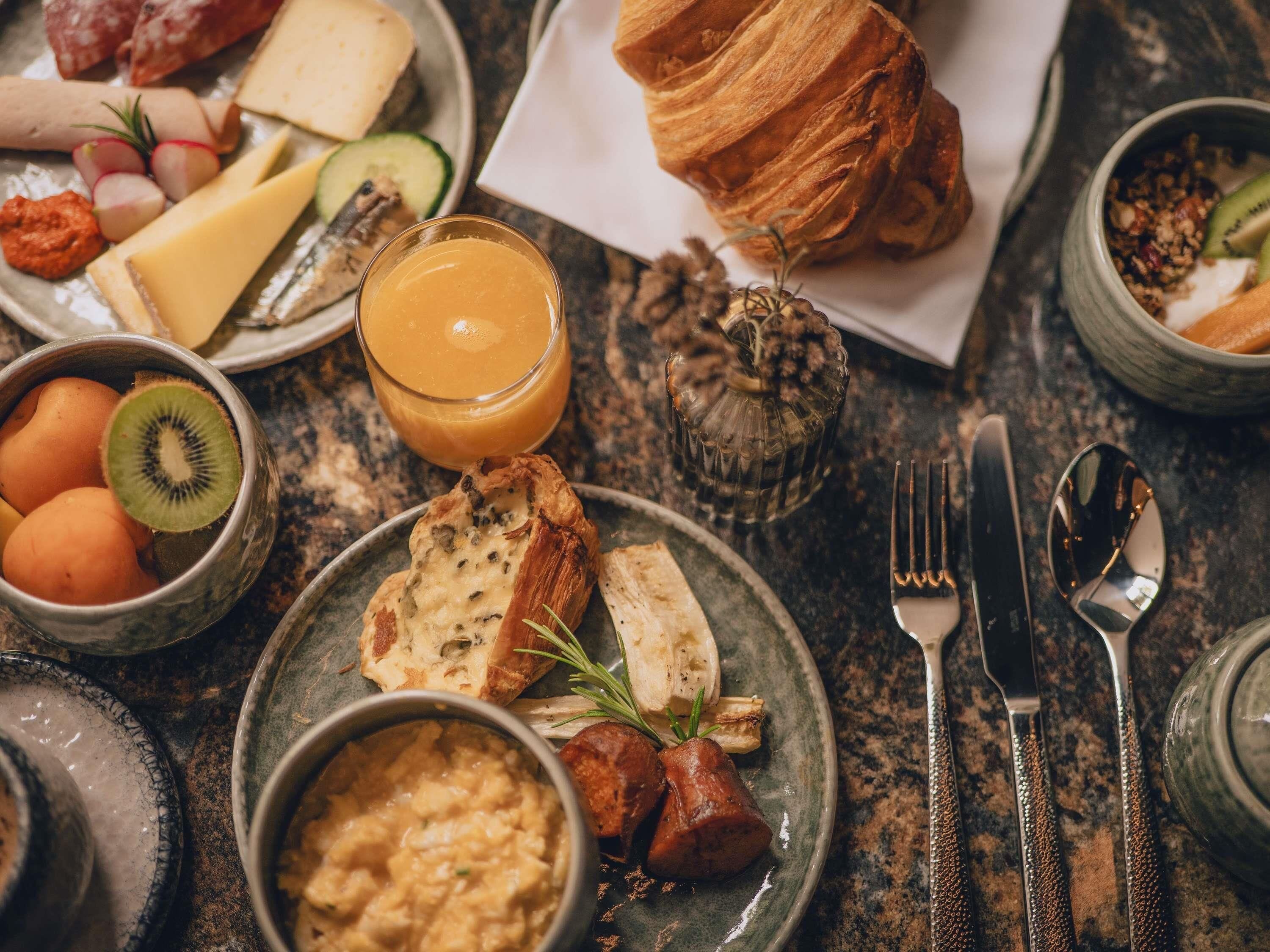 Uma mesa de café da manhã com diversos alimentos, como queijo, pão e um croissant.