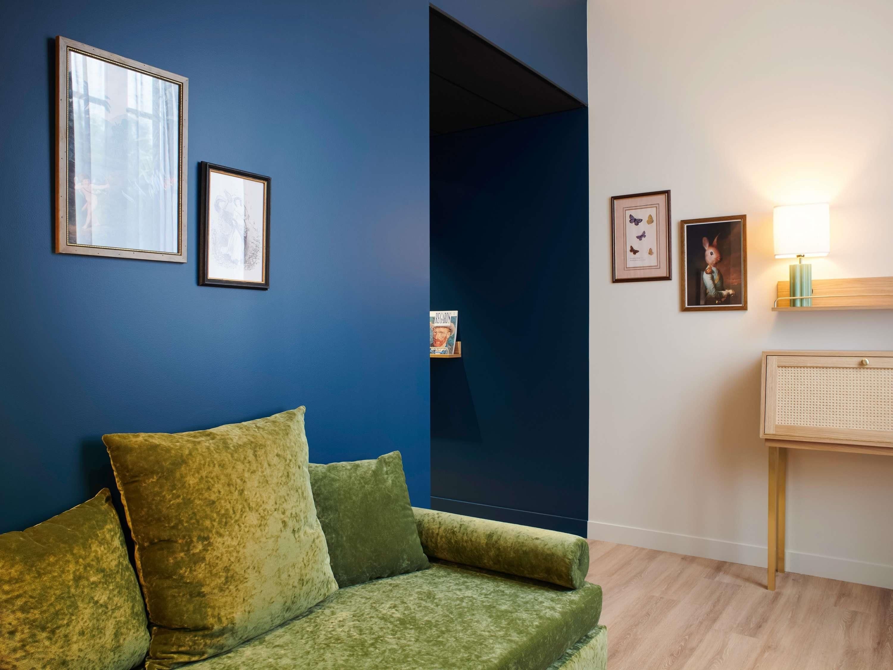 Um quarto com um sofá verde, uma mesa de apoio de madeira e quadros nas paredes.