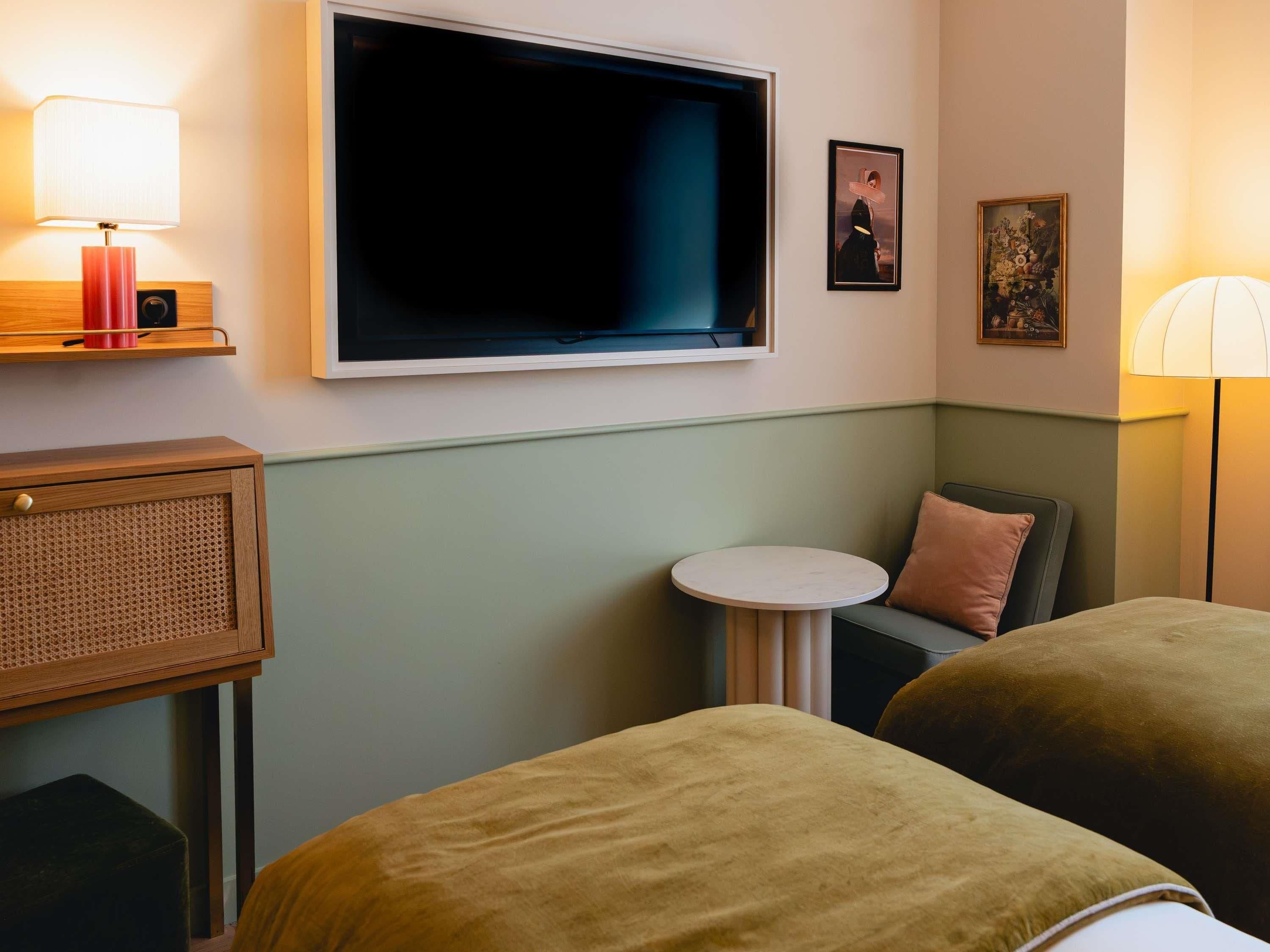 Quarto de hotel com duas camas, uma mesa redonda pequena, televisão e abajur.
