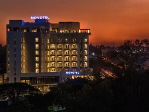 Um hotel de vários andares com uma placa grande 'NOVOTEL', várias varandas e uma fachada bem iluminada.