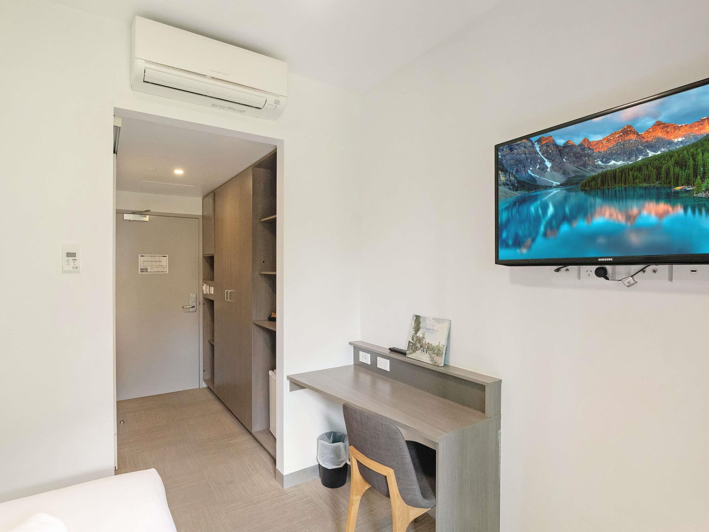 Quarto de hotel moderno com uma televisão de tela plana grande fixada na parede, uma escrivaninha de madeira e um espaço de estar acolhedor.
