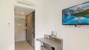 Quarto de hotel moderno com uma televisão de tela plana grande fixada na parede, uma escrivaninha de madeira e um espaço de estar acolhedor.