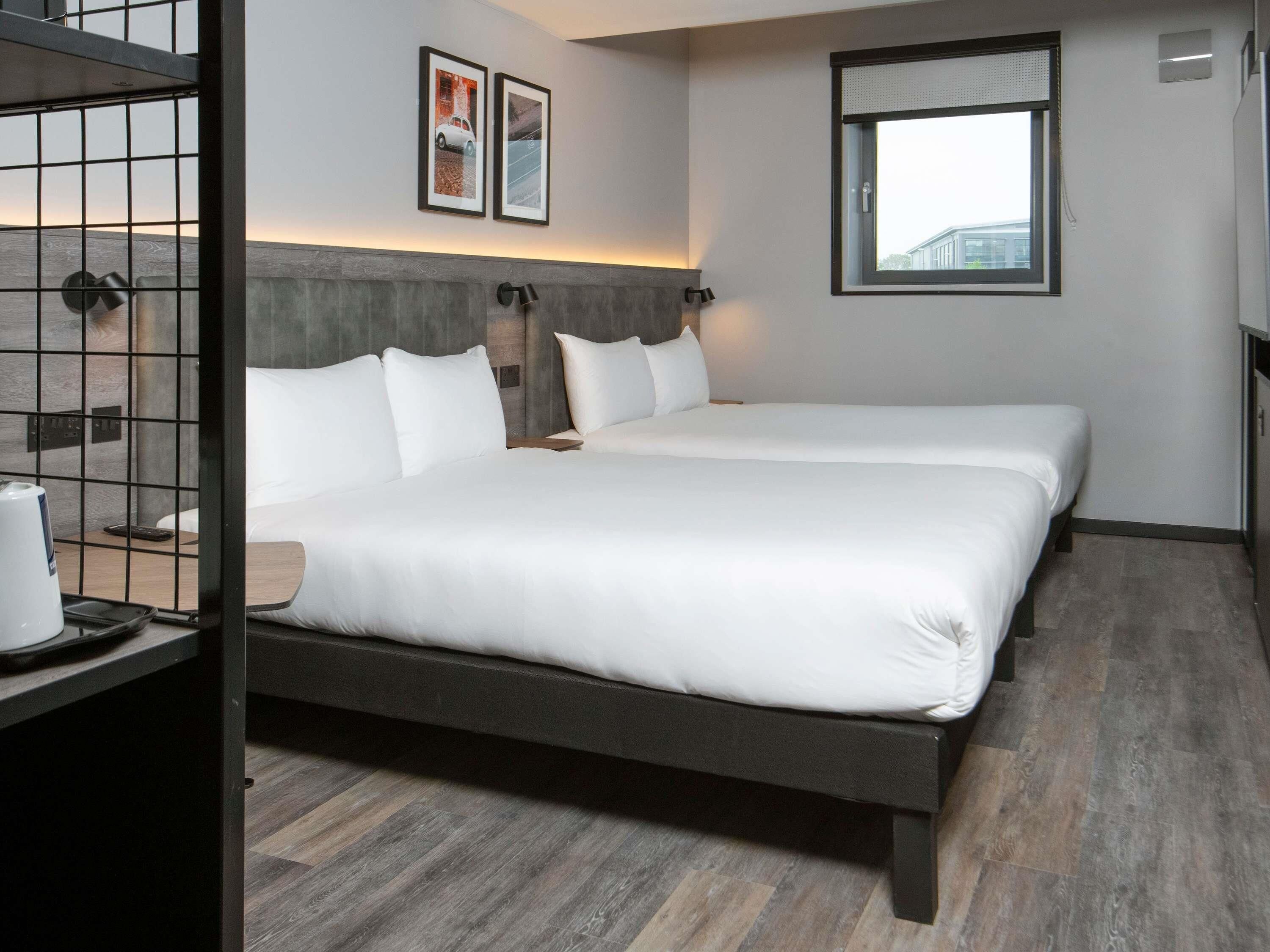 Quarto de hotel com duas camas, uma janela e vista para um edifício.