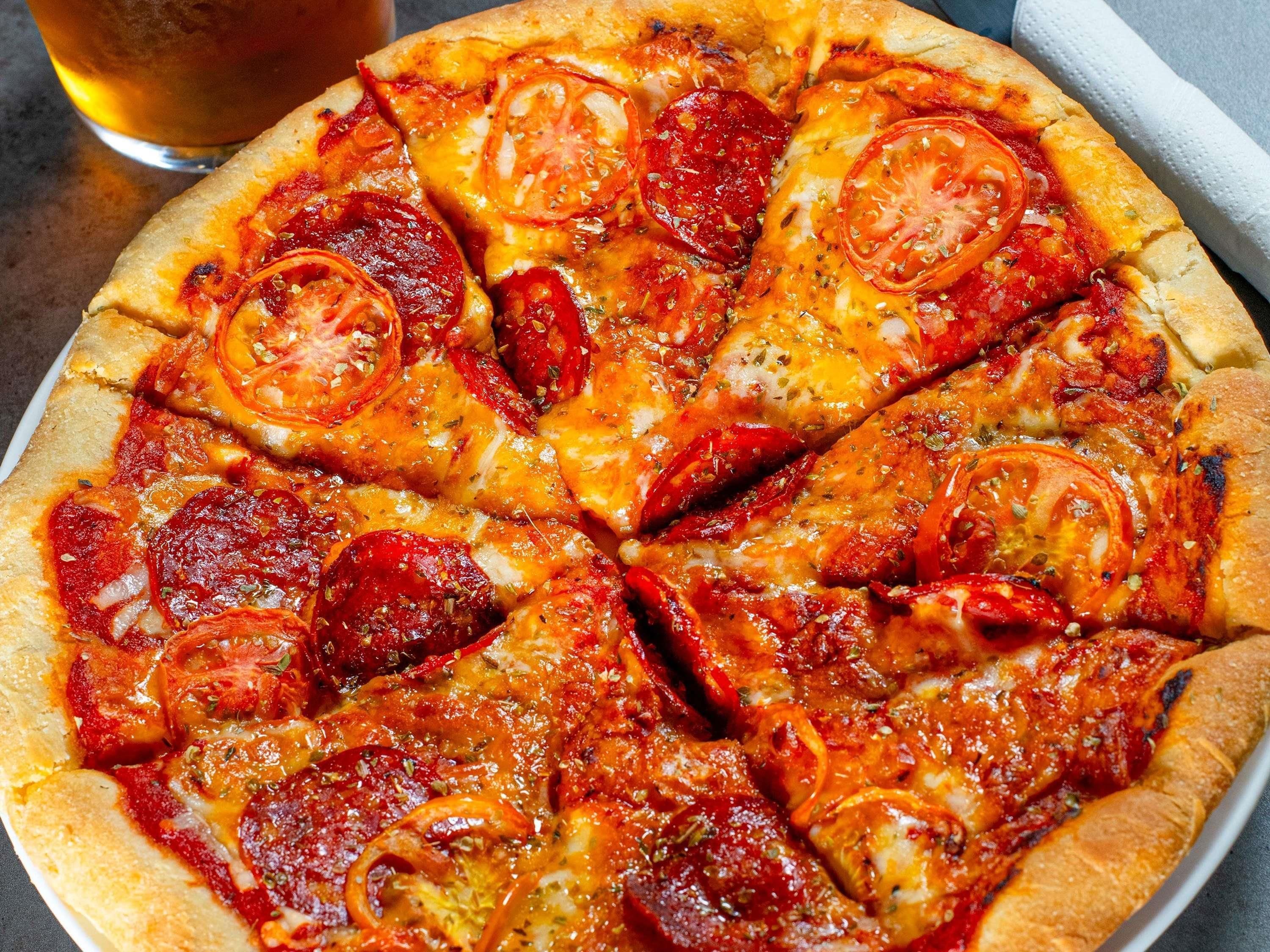 Pizza com fatias de tomate e pepperoni em um prato branco.