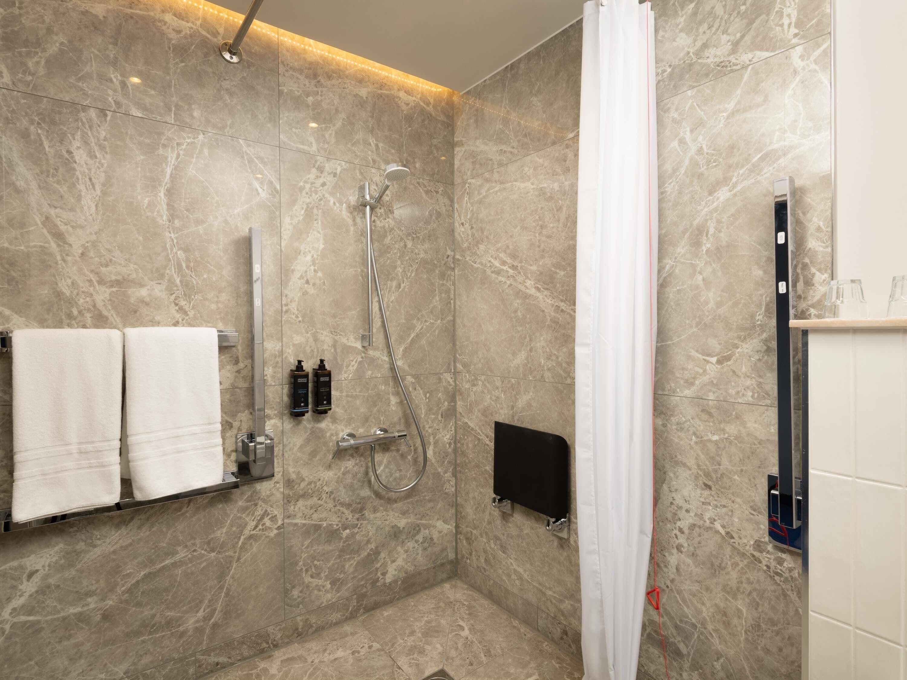 Um banheiro moderno com piso de mármore, chuveiro com chuveiro manual, porta-toalhas com duas toalhas e um dosador de sabonete preto.