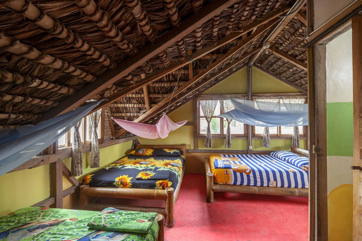Quarto com duas camas, um tapete vermelho e um telhado de palha.