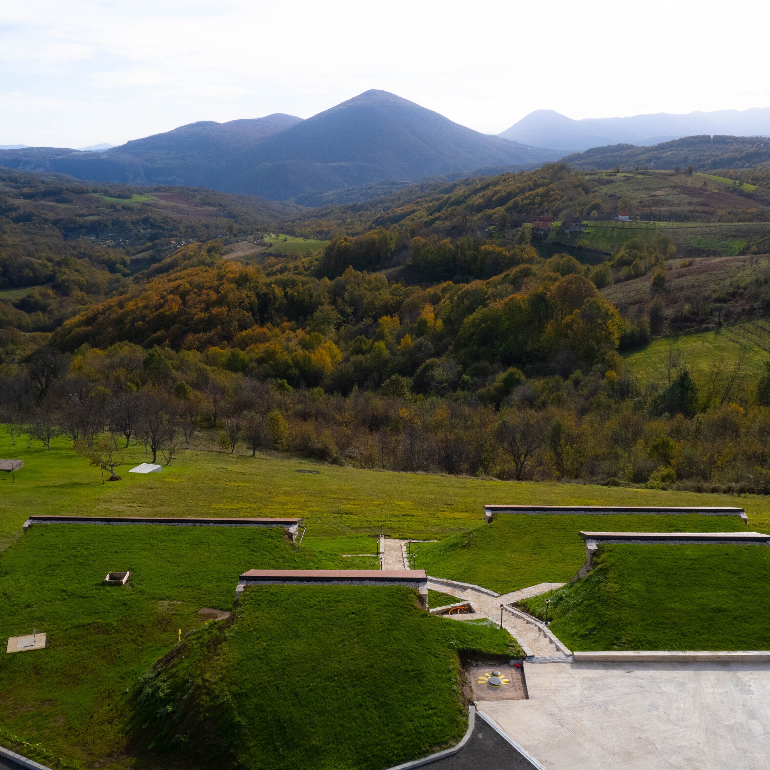 Vista panorâmica de uma paisagem montanhosa com uma área de parque, incluindo caminhos e um pequeno edifício.