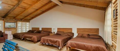 Quarto em estilo cabana de tronco com três camas de madeira, um banco azul e teto de madeira.