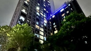 Um edifício alto com várias janelas iluminadas e uma luz azul característica na lateral.