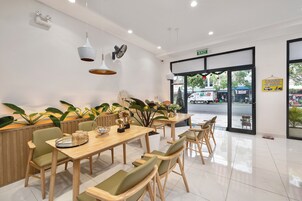 Um restaurante moderno com mesas e cadeiras de madeira, plantas em vasos e um interior limpo e bem iluminado.