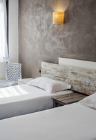 Quarto de hotel com duas camas, uma cadeira branca, parede texturizada e luminária fixada na parede.