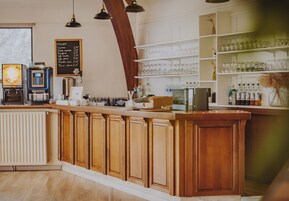 Uma área de bar com armários de madeira, uma máquina de café e prateleiras com copos e garrafas.