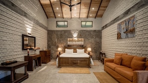 Quarto com uma cama grande, duas mesas de cabeceira, um criado-mudo, um banco de madeira e um sofá marrom.