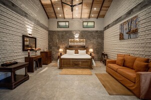 Quarto com uma cama grande, duas mesas de cabeceira, um criado-mudo, um banco de madeira e um sofá marrom.